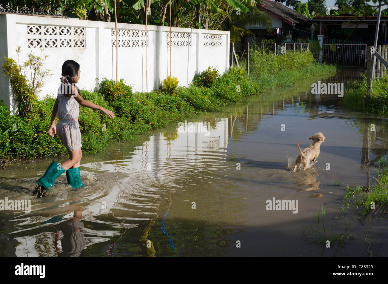 Young Girl Wearing Rubber Boots Walks Across Flooded Road With A Stock