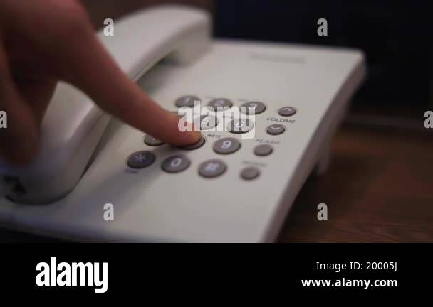 Male hand pushes buttons on a white landline telephone placed on a ...