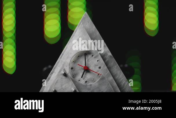 A clock is on top of a pyramid shaped structure. The clock is set at 12 ...