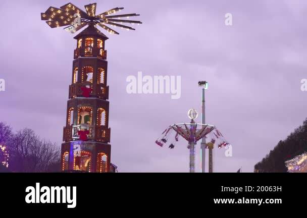 A glowing Christmas pyramid stands next to a vibrant carnival ride at a ...