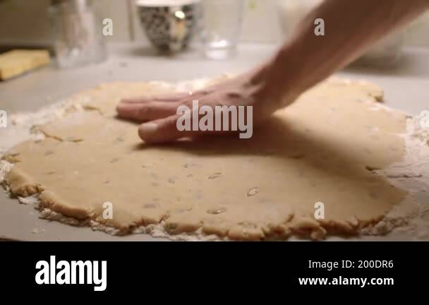 A person rolling out cookie dough on a floured surface, preparing to ...