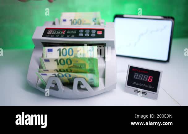 Cash counting machine switched on stands on the desk. Hand touches a ...