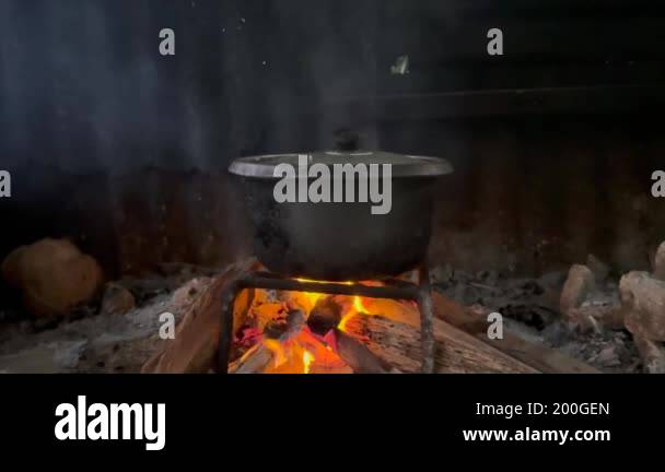 Rustic cooking setup featuring a black pot on a firewood stove with ...