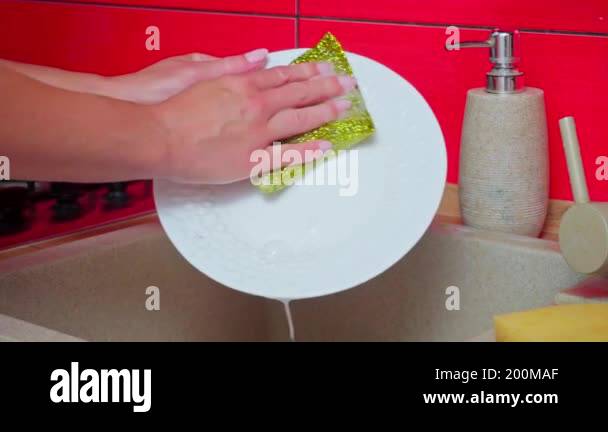 A hand is scrubbing a plate in a modern, stylish kitchen, demonstrating ...