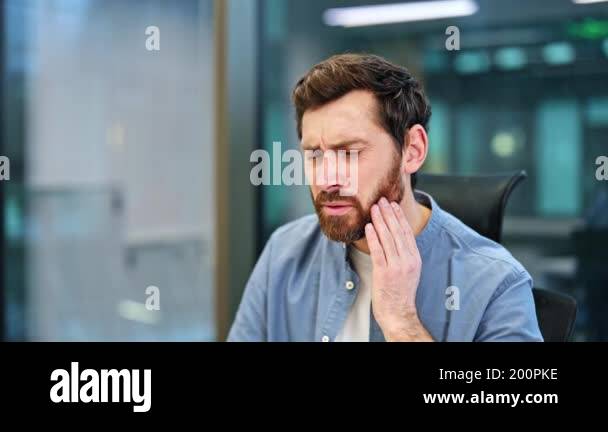 Bearded man in blue shirt sitting in office chair experiencing intense ...