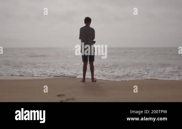 Teen standing in ocean waves, feeling the water crash around his feet ...
