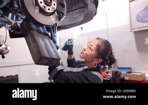 Skilled female mechanic inspecting a car wheel with flashlight in a ...