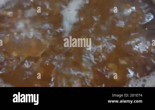 A detailed close-up of a boiling brown liquid with visible bubbles and ...