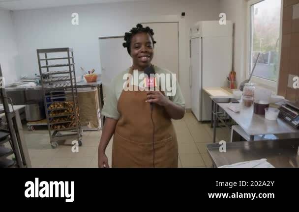 Medium shot of cheerful Black female chef in brown apron speaking in ...