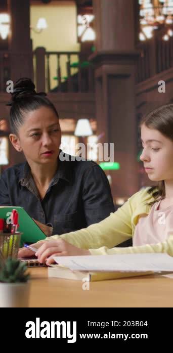 Vertical Video Female tutor mentoring schoolgirls in a school library ...
