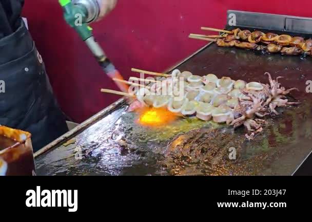 cook grills skewered squid over an open flame using a blowtorch ...