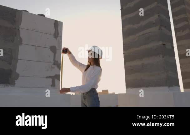 Female engineer measuring wall with tape measure at construction site ...