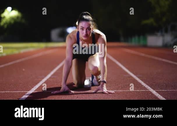 Female Runner on Athletics sprint race starting blocks on a dark ...