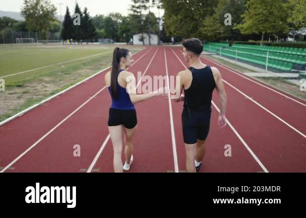 The sporty athletics couple is done jogging around the stadium. They are walking on the sports ...