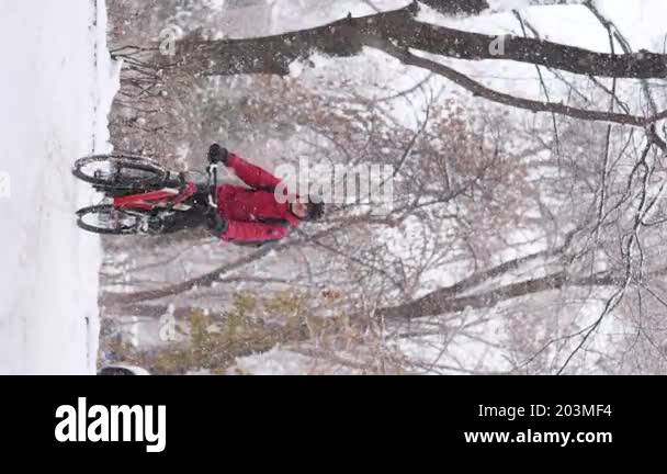 Vertical video footage of a man rides a bicycle in winter in a snowfall ...