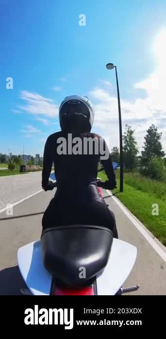 Rear view of a Caucasian woman riding an electric motorcycle. Vertical ...