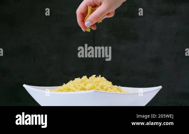 Close-up of womans hand with a bunch of pasta falling into a bowl ...