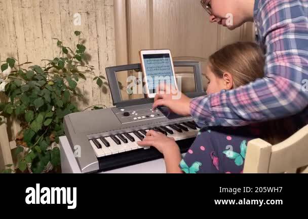 A young music teacher guides a child in learning to play the digital ...