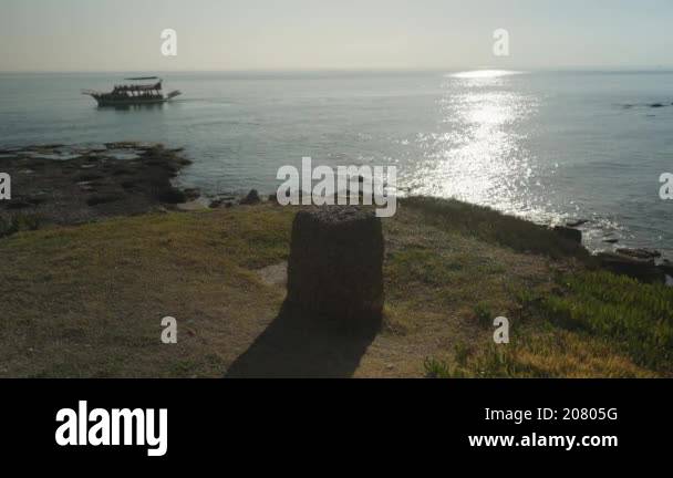 A lone stone pillar on a grassy hilltop near the sea, with sunlight ...