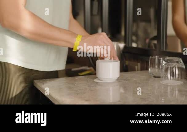A woman stirs her drink in a white cup while standing in a modern ...