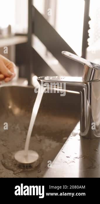 Vertical video. A close-up of a woman washing her hands under a sleek ...