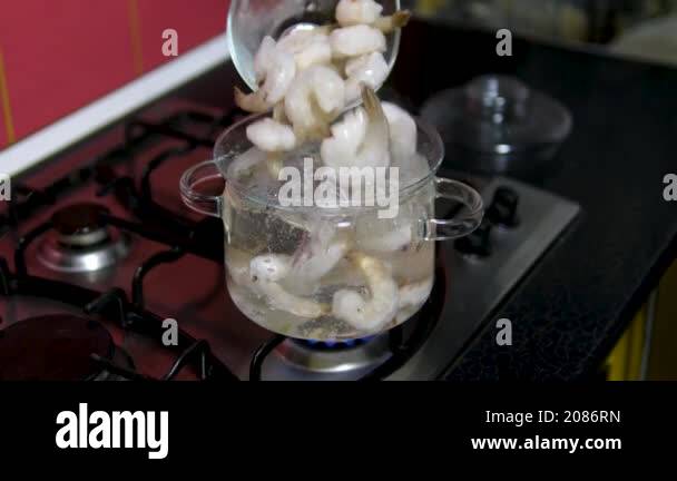 Person cooking prawns in a pot on a gas stove. The focus on the hands ...