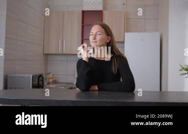 Young woman leans on her kitchen counter, resting her chin on her hand ...