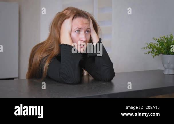Young woman sits at her kitchen counter, struggling with intense ...