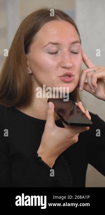 Businesswoman sits at desk, recording voice message on her smartphone ...