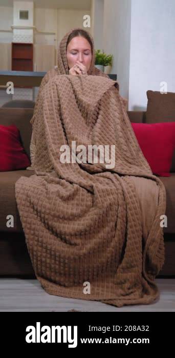 Woman wrapped in knitted blanket sits alone, shivering from cold, on ...