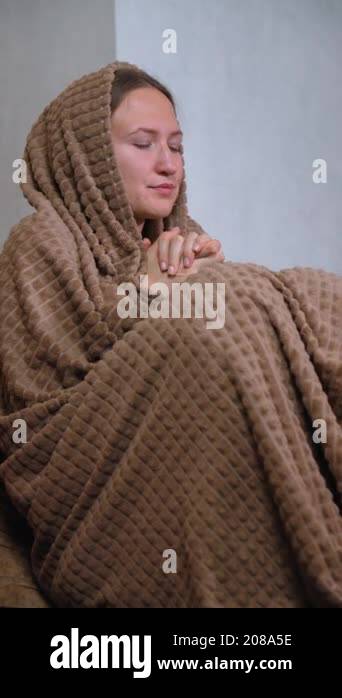 Woman wrapped in knitted blanket sits alone, shivering from cold, on ...