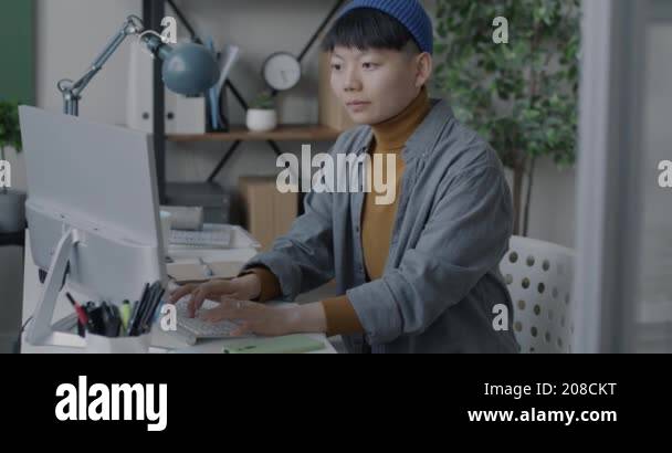 Portrait of young Asian man working with computer typing then turning ...