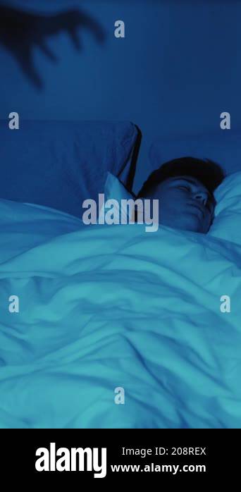 Vertical video. Scary shadow hand hovers over scared sleeping guy in ...