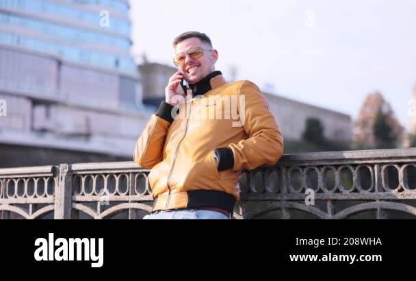 A young man wearing a bright yellow jacket enjoys a phone call while ...