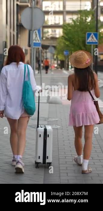 On a sunny day, two young women leisurely stroll down a bustling city ...
