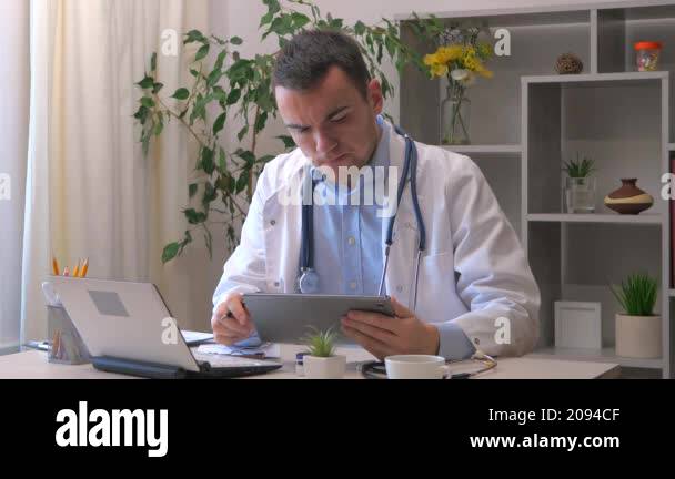 A young intern doctor works in an office, studies a patient's medical ...