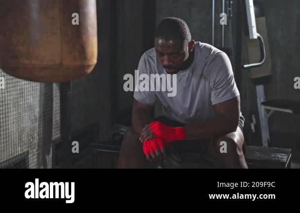 Boxer in gym. Tired African man fighter with red boxing wraps resting ...