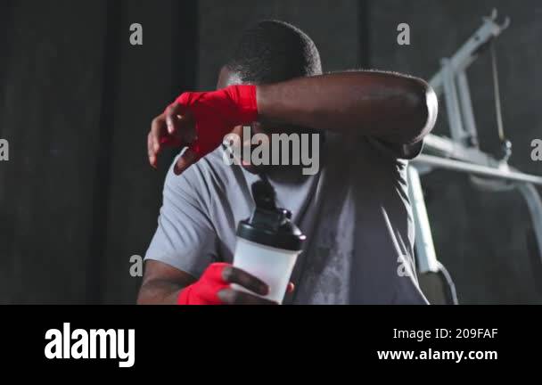 Boxer in gym. Tired African man fighter with red boxing wraps wipes ...