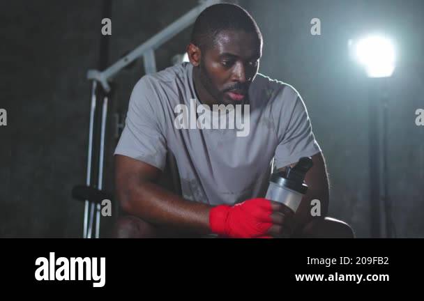 Boxer in gym. Tired African man fighter with red boxing wraps resting ...