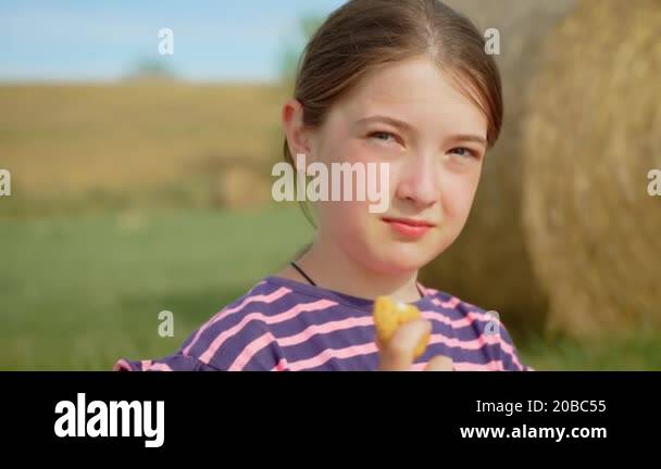 Happy girl enjoying chicken nuggets outdoors during sunny picnic. Young ...