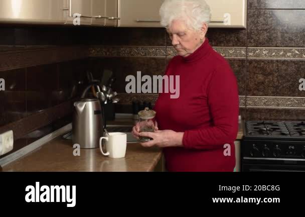 Elderly woman pours pours loose black tea into cup. Old female ...