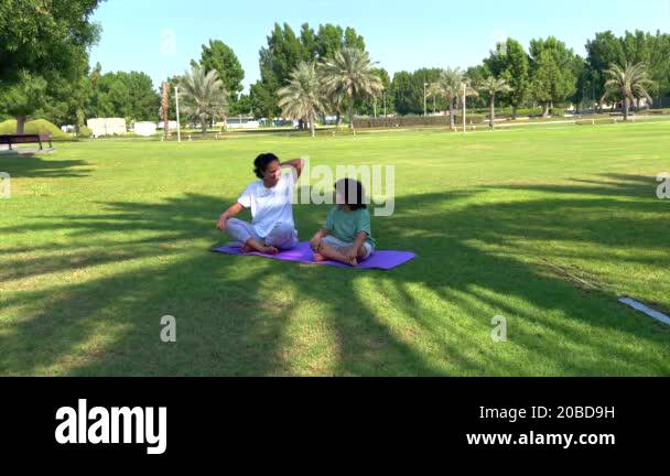 Mother-child practice yoga on mats under sunlight, park setting highlighting calm exercise ...