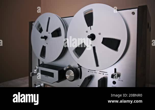 A vintage reel-to-reel tape recorder in action, with a hand adjusting ...