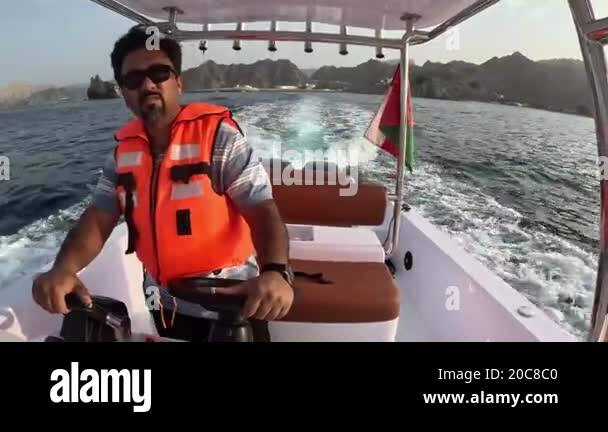 Close-shot of man in an orange life jacket steering confidently a boat ...