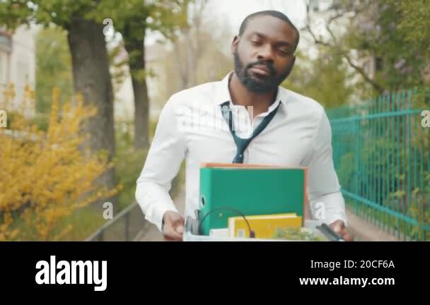 Serious African american office worker man walking with box of personal ...