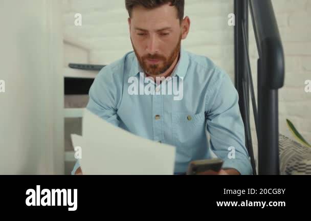 Unhappy businessman working with smartphone and documents on sofa holds ...