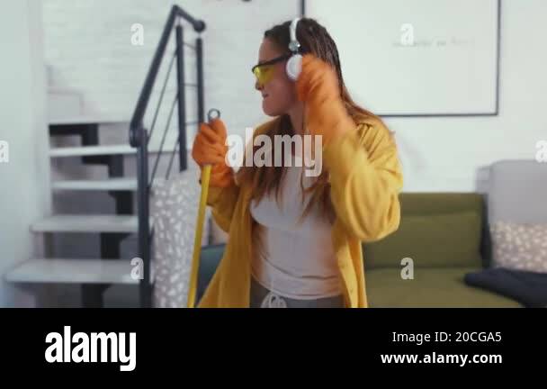 Funny young lady is having fun during clean-up singing and dancing with ...
