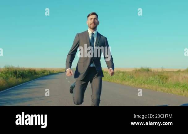 Funny businessman runs skipping along a country road near a wheat field freedom concept outdoors ...