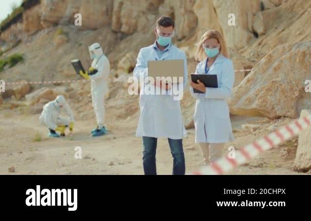 Ecology experts use laptop in protection mask working on land relief chemicals and toxic samples ...