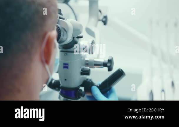 NEW YORK - April 5, 2020: Shot of dentist man with dental microscope with assistant and man as ...